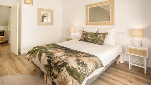 Quarto com cama, duas mesas de cabeceira com luminárias, um espelho grande sobre a cama e uma porta que dá para outro cômodo.