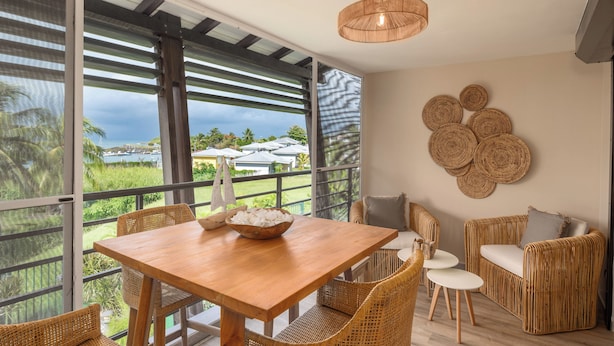 Uma varanda com mesa de madeira, cadeiras de vime e vista para uma piscina e vegetação.