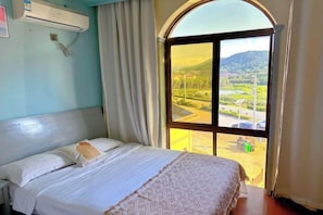 Quarto de hotel com cama, janela com vista para paisagem e ar condicionado na parede.