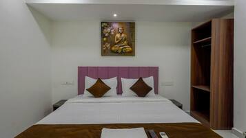 Quarto de hotel com cama, cabeceira, quadro, guarda-roupa e controle remoto sobre a cama.