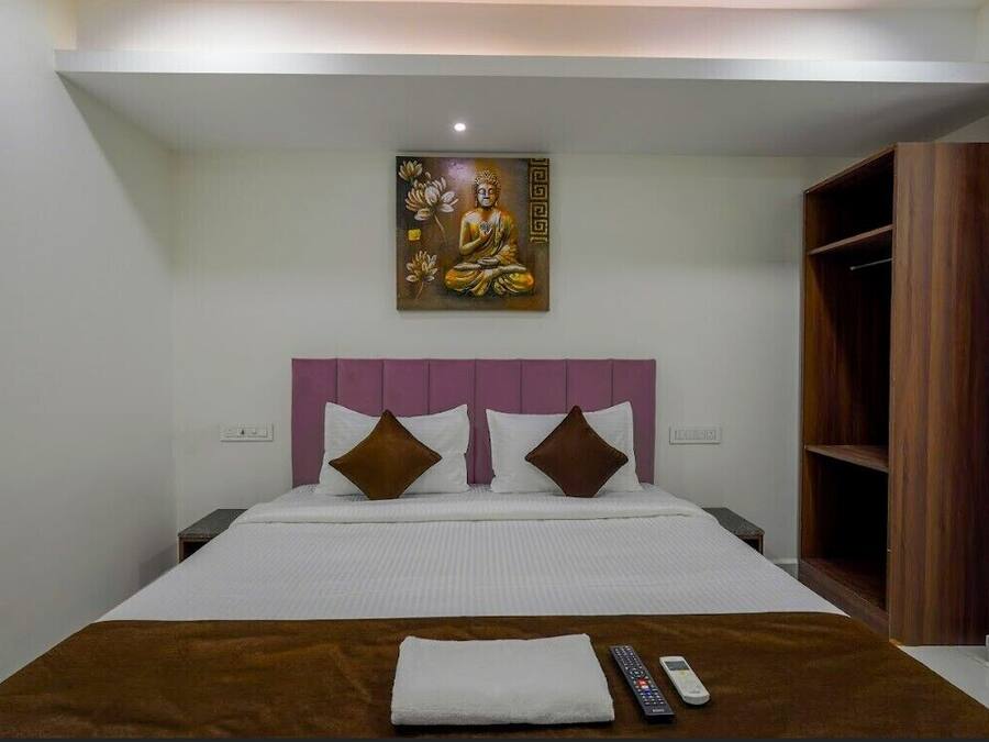 Quarto de hotel com cama, cabeceira, quadro, guarda-roupa e controle remoto sobre a cama.