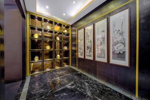 Um corredor com piso de mármore, obras de arte nas paredes e uma vitrine iluminada.