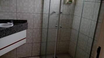 Uma casa de banho com chuveiro em cabine de vidro, pia com bancada de mármore e sanita.