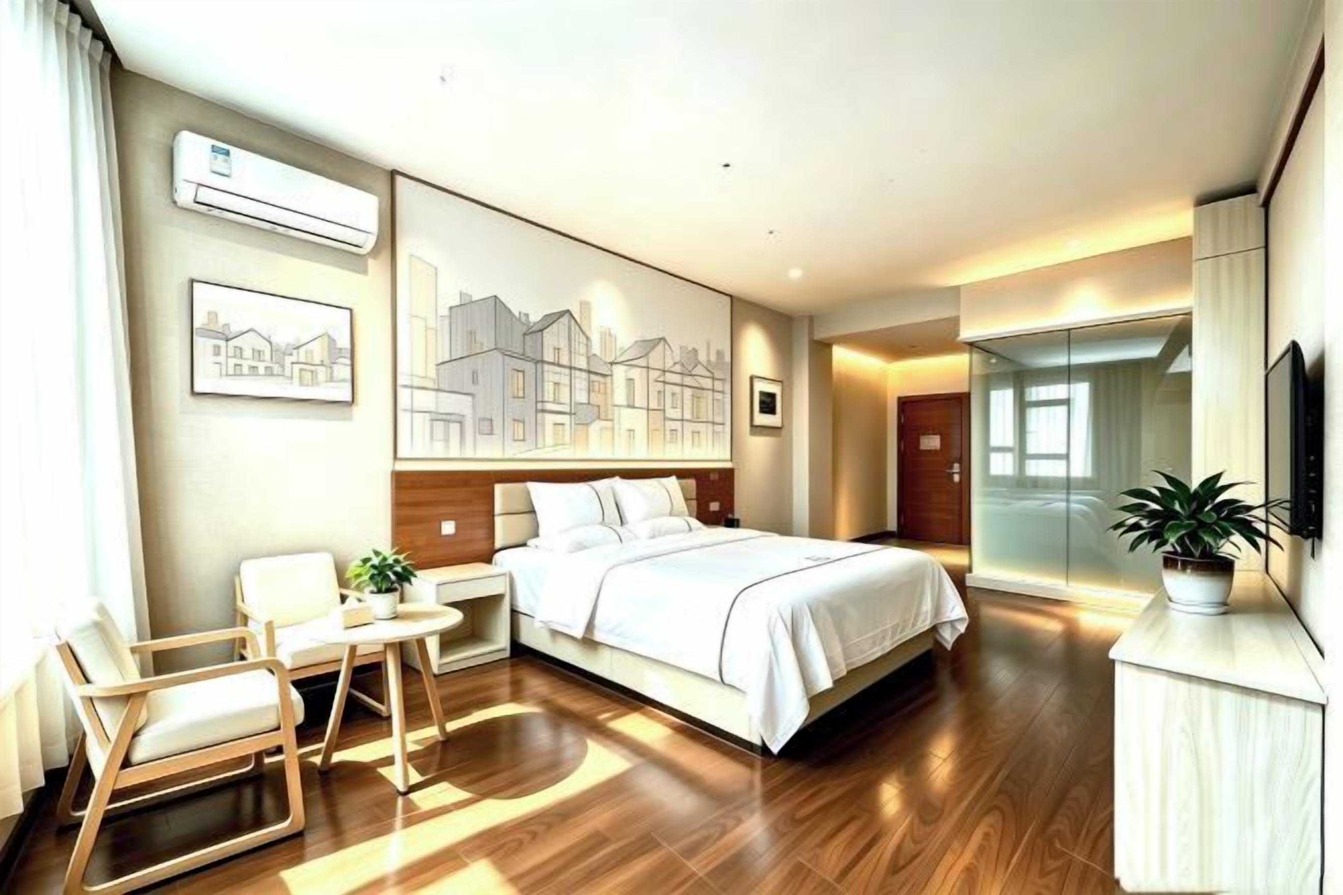 Quarto de hotel com cama, escrivaninha, cadeira, planta em vaso e uma obra de arte com vista para a cidade na parede.