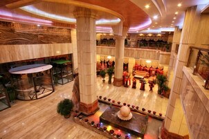 Um saguão de hotel com piso de mármore, uma fonte central e diversas áreas de estar.