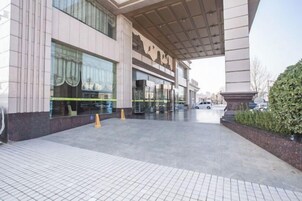 Entrada de hotel com galeria coberta, porta de vidro e área de estacionamento.