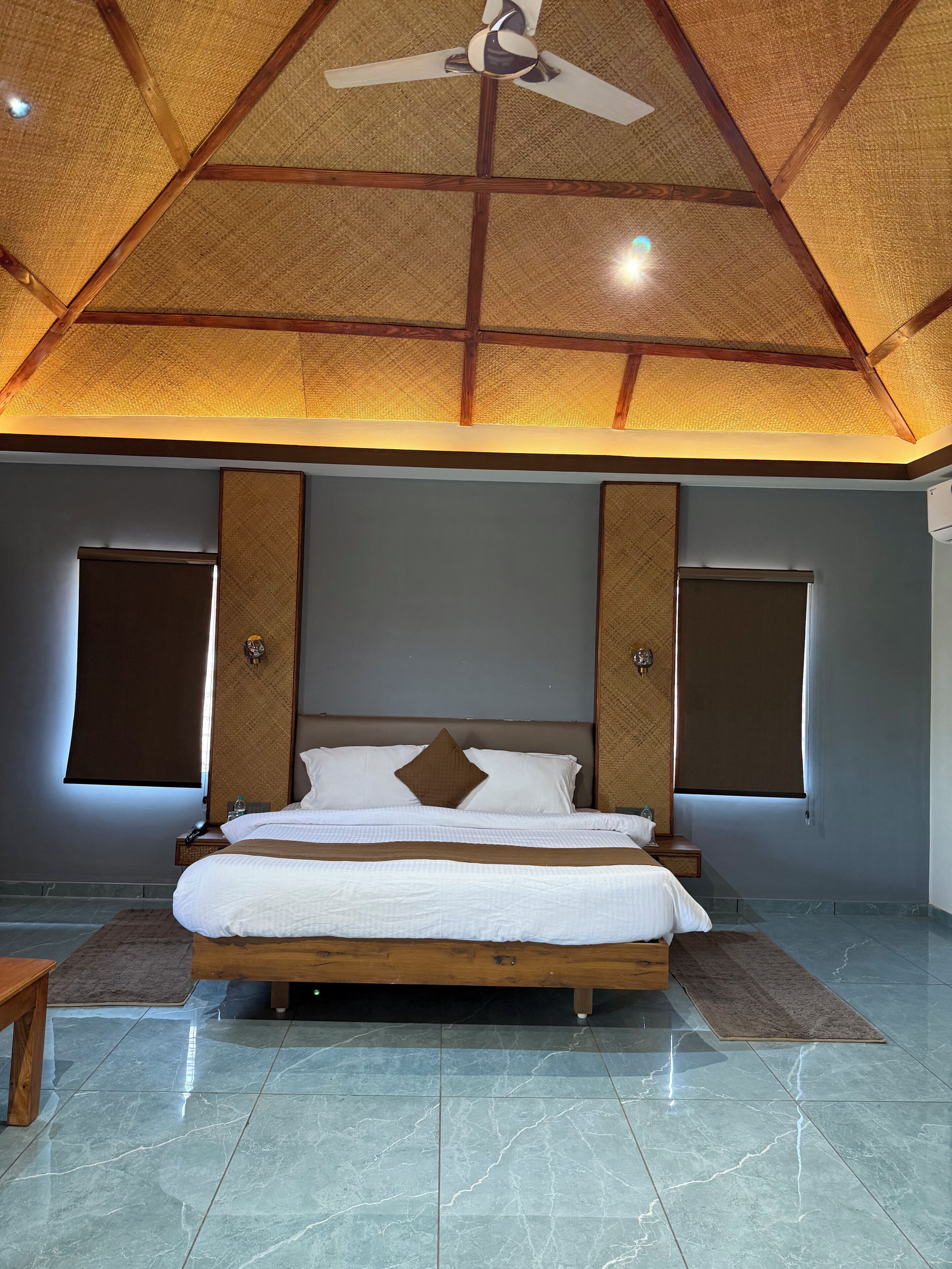 Quarto com cama grande, ventilador de teto e vista para o céu pela janela.
