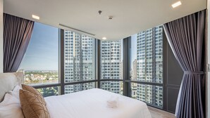 Quarto de hotel moderno com uma cama grande, vista para edifícios altos e uma varanda com cortinas.