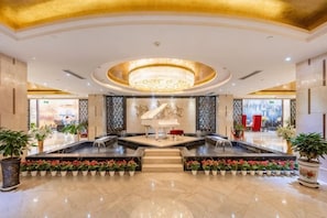 Um saguão de hotel com um lustre imponente, um piano e uma área de estar central.
