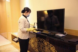 Uma pessoa limpando uma televisão de tela plana em quarto de hotel.