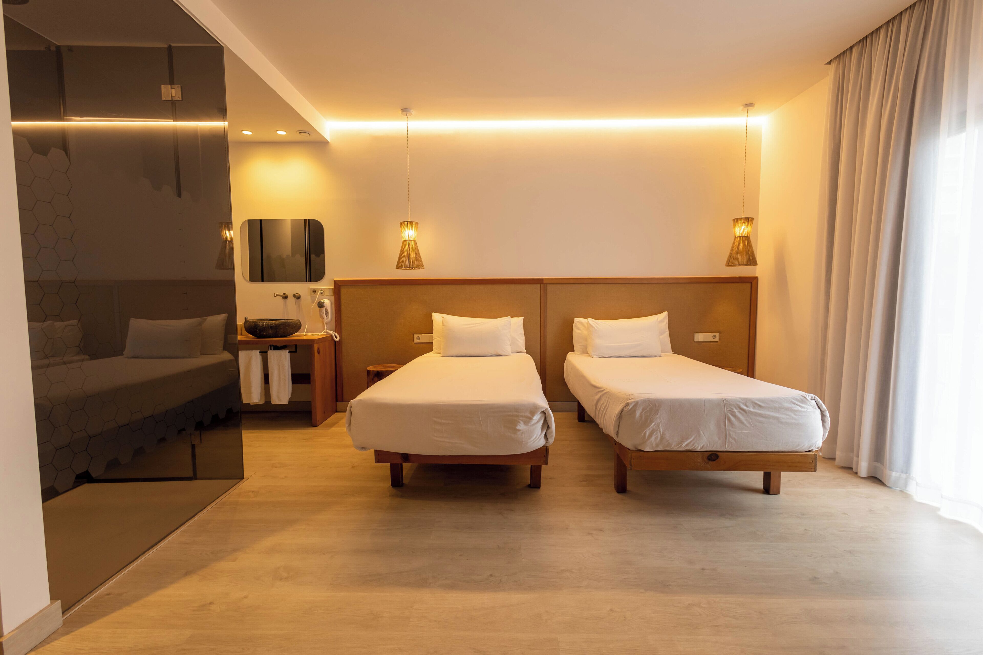 Quarto de hotel com duas camas, um sofá, um espelho e uma mesinha.