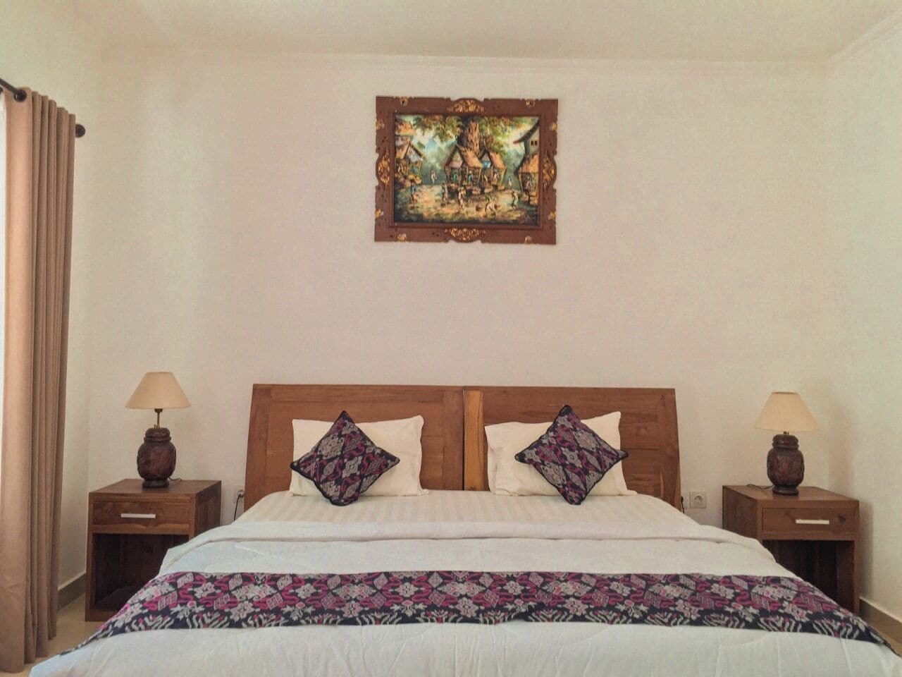 Cama bem arrumada com colcha florida, duas almofadas iguais e duas luminárias em mesas de cabeceira de madeira.