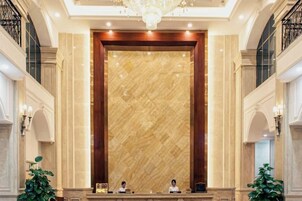 Uma área de recepção com parede de mármore, um lustre e dois recepcionistas atrás do balcão.