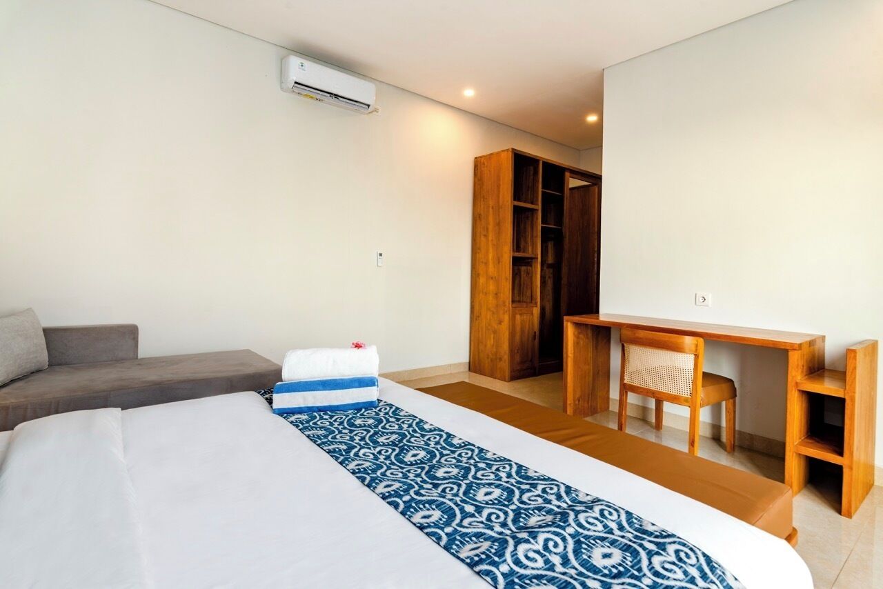 Quarto de hotel com uma cama, uma escrivaninha, uma cadeira, um guarda-roupa e um ar condicionado.