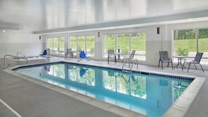 Piscina interna com vista desimpedida para o exterior, cercada por cadeiras e mesas.