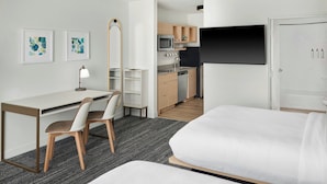 Quarto de hotel moderno com escrivaninha, duas cadeiras, cama, televisão e cozinha.