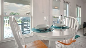Uma mesa de jantar com cadeiras brancas, um copo e uma tigela sobre um pano de mesa branco.