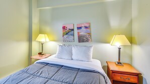 Cama bem arrumada com edredom azul e branco, duas luminárias de mesa e duas quadros pendurados na parede.