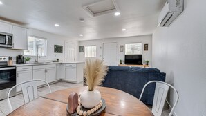 Uma cozinha moderna com armários brancos, uma mesa de jantar com um vaso e objetos decorativos, e um sofá azul ao fundo.