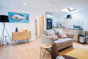 Uma sala de estar moderna com um sofá, uma pequena mesa lateral, um armário de madeira e um quadro de um peixe na parede.