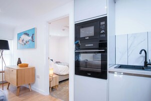 Uma cozinha moderna com forno embutido e micro-ondas, uma pequena mesa lateral de madeira e uma pintura na parede.
