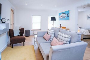 Uma sala de estar moderna com um sofá cinza, uma poltrona marrom, uma mesa de centro e um quadro na parede.