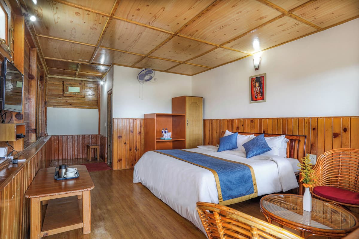 Quarto com decoração em madeira, com uma cama, uma mesa com xícara e pires, uma cadeira de vime e um pequeno armário.