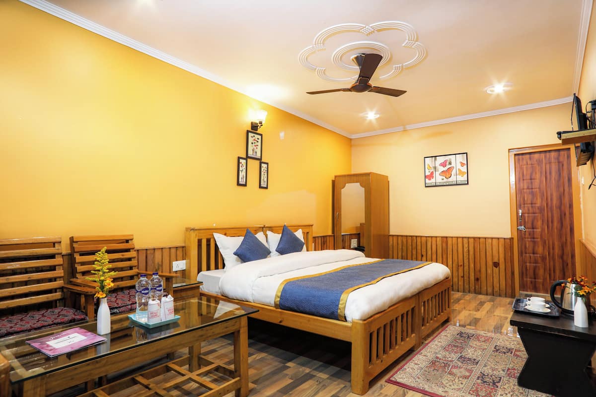 Quarto de hotel com cama de madeira, mesa de vidro, banco de madeira, porta de madeira e ventoinha no teto.