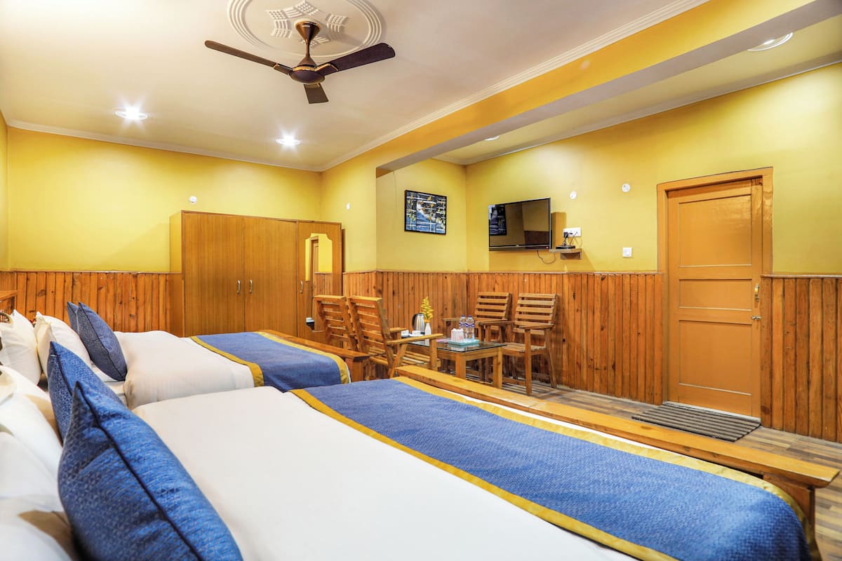 Quarto de hotel com duas camas, mobiliário de madeira, televisão e ventoinha no teto.