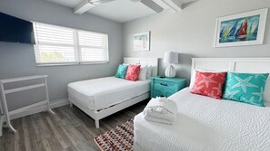 Quarto com duas camas, mesa de cabeceira, luminária, televisão e obras de arte nas paredes.