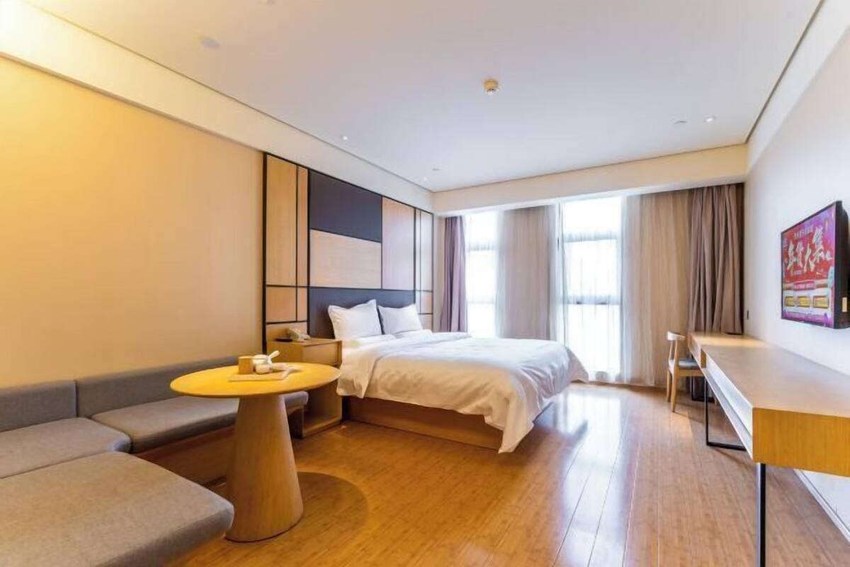 Quarto de hotel moderno com uma cama, uma pequena mesa redonda, um sofá e uma escrivaninha.