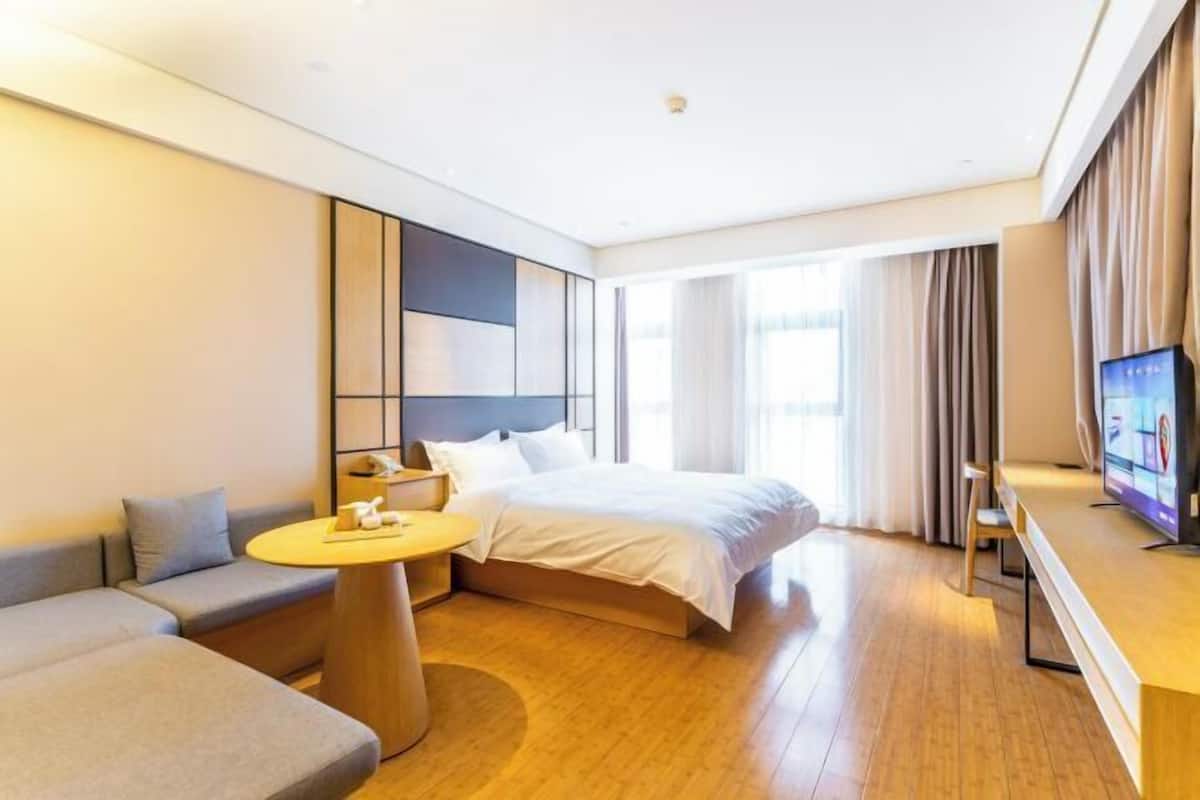 Quarto de hotel moderno com uma cama grande, um sofá, uma mesa redonda pequena e uma televisão.