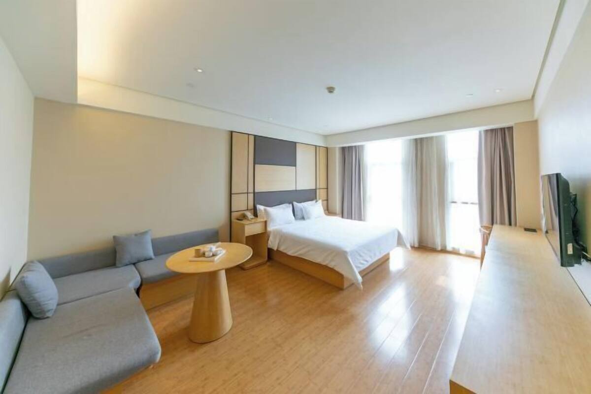 Quarto de hotel moderno com cama, sofá, mesa redonda e televisão.