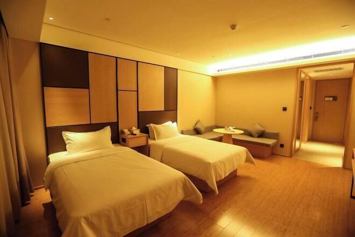 Quarto de hotel com duas camas, um sofá e uma mesinha.
