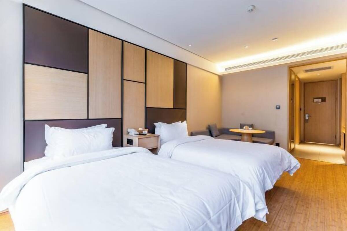 Quarto de hotel com duas camas, uma mesinha e uma porta.
