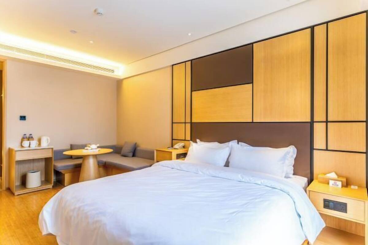 Quarto de hotel moderno com uma cama grande, mesas de cabeceira, um pequeno espaço para sentar e um design de painel na parede.