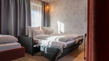 Quarto de hotel moderno com cama adaptável, área de estar separada e uma grande janela com cortinas.