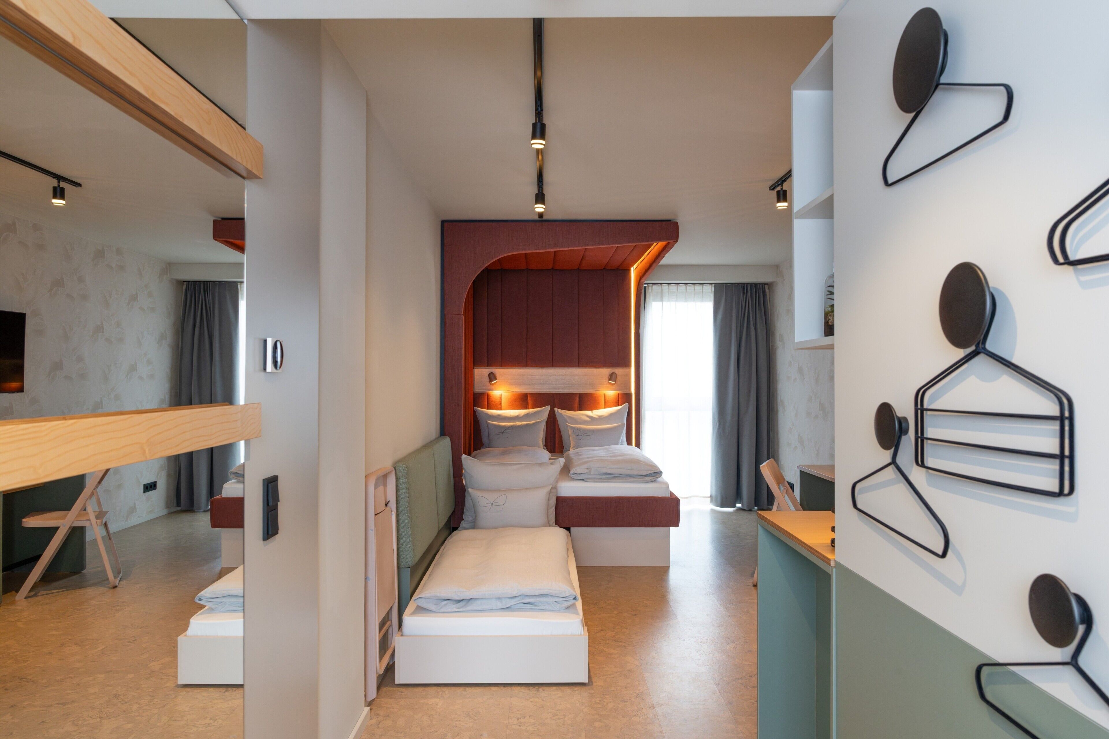 Quarto de hotel moderno com uma cama, mesas de cabeceira, uma escrivaninha e luminária fixada na parede.