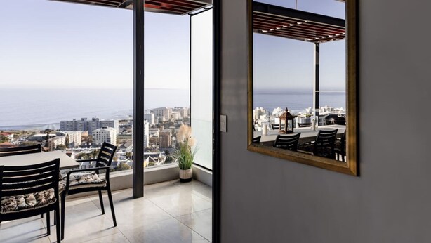 Uma varanda com vista para a cidade e o oceano, uma mesa de jantar com cadeiras e um espelho grande na parede.