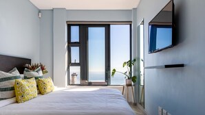 Quarto de hotel moderno com uma cama grande, televisão de tela plana na parede e uma janela ampla com vista para o horizonte da cidade.