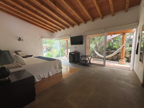 Quarto com cama, televisão, escrivaninha e vista para um jardim através de uma porta de correr de vidro.