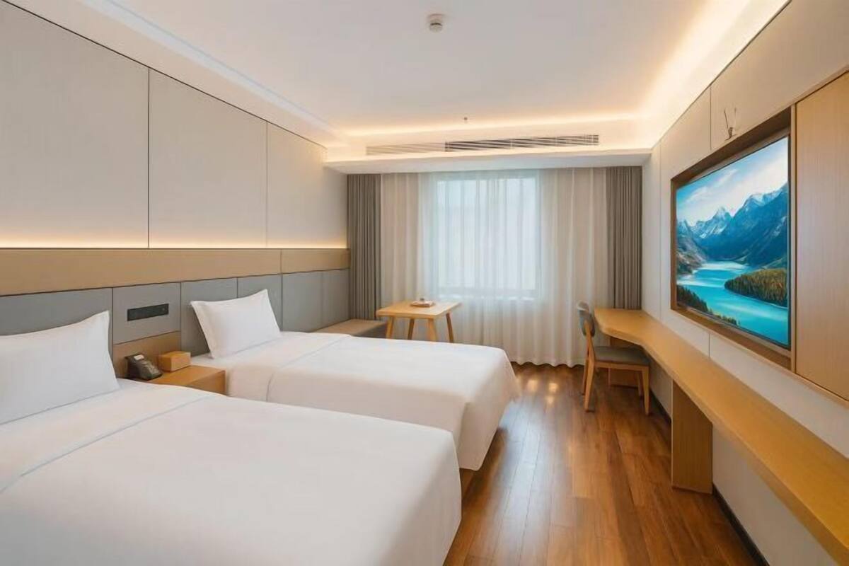 Quarto de hotel com duas camas, uma escrivaninha, uma cadeira, uma televisão e uma janela com cortinas.