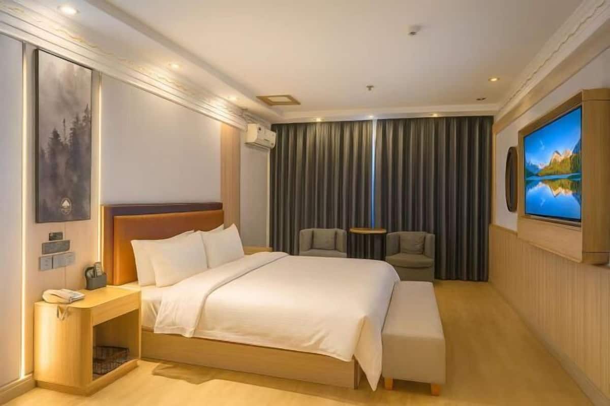 Quarto de hotel moderno com uma cama grande, televisão, um pequeno espaço de estar e um quadro na parede.