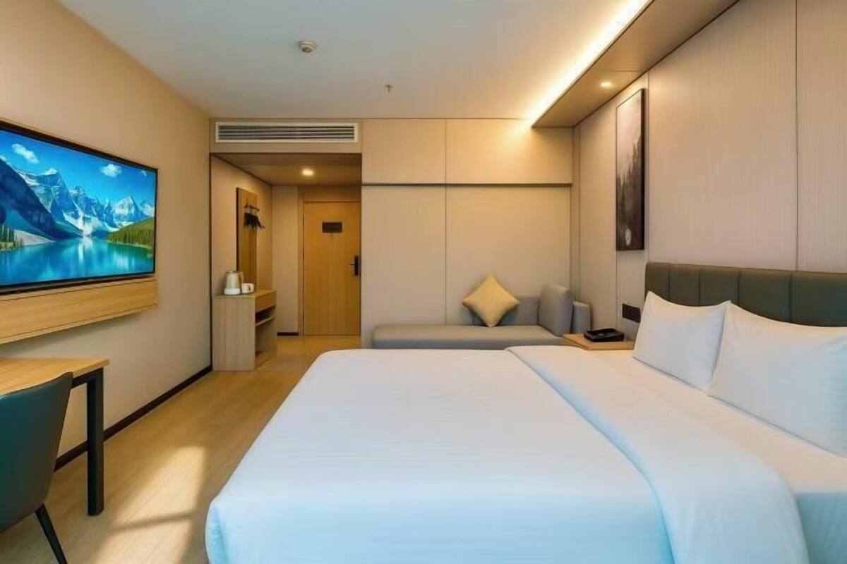 Quarto de hotel moderno com uma cama grande, uma escrivaninha, uma televisão e vista para um lago montanhoso.