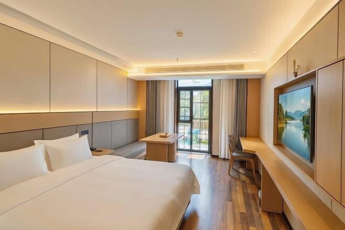 Quarto de hotel com cama grande, uma mesa, televisão e vista para o exterior.