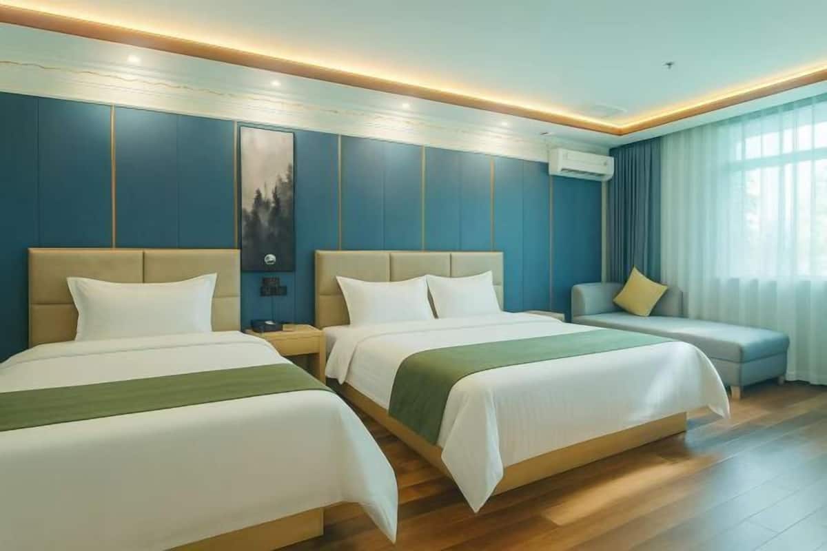 Quarto de hotel com duas camas, um sofá e uma janela grande com cortinas.