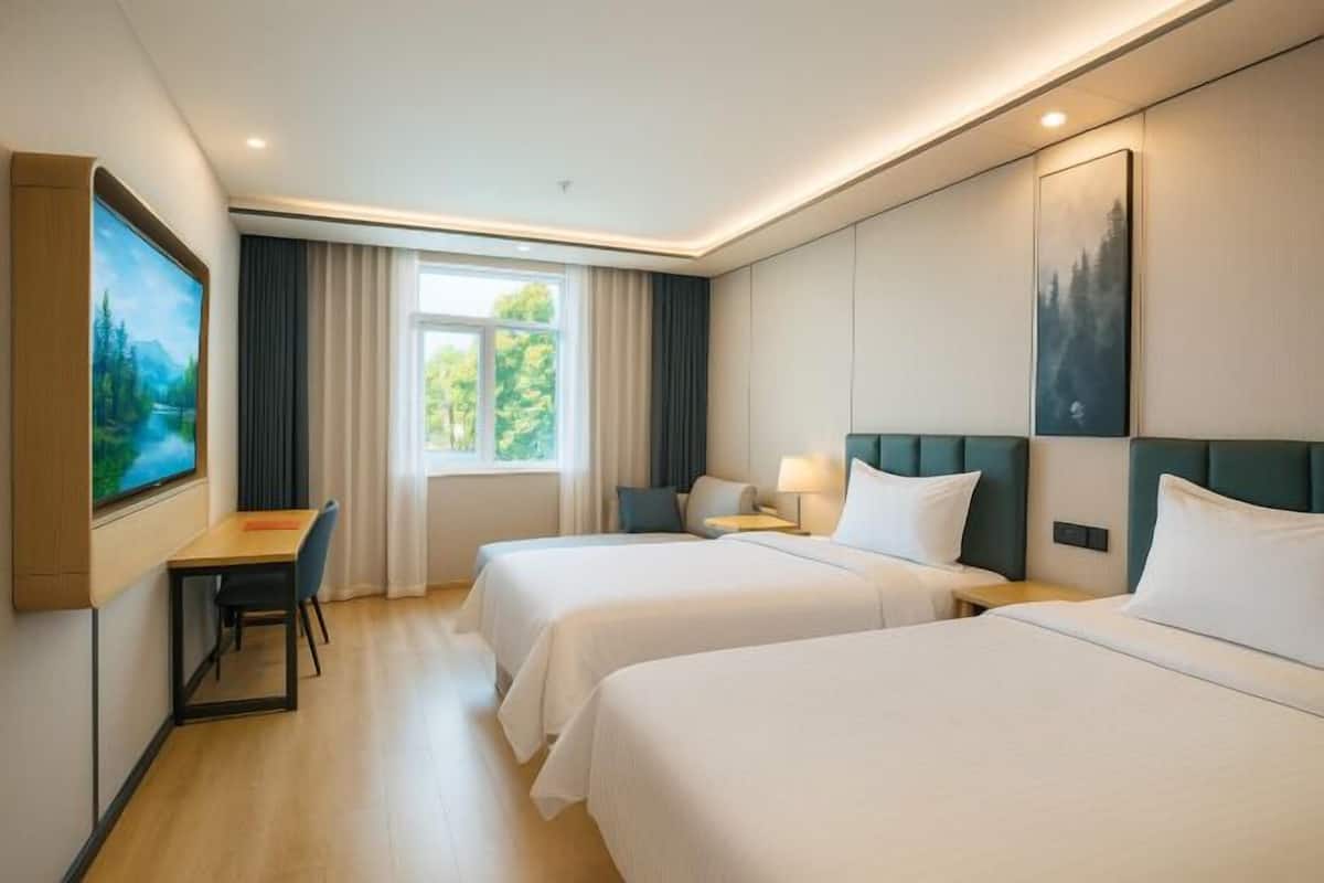 Quarto de hotel com duas camas, uma mesa e uma janela com cortinas.