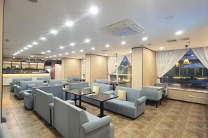 Um saguão de hotel com áreas de estar, balcão de recepção e vista para o exterior.