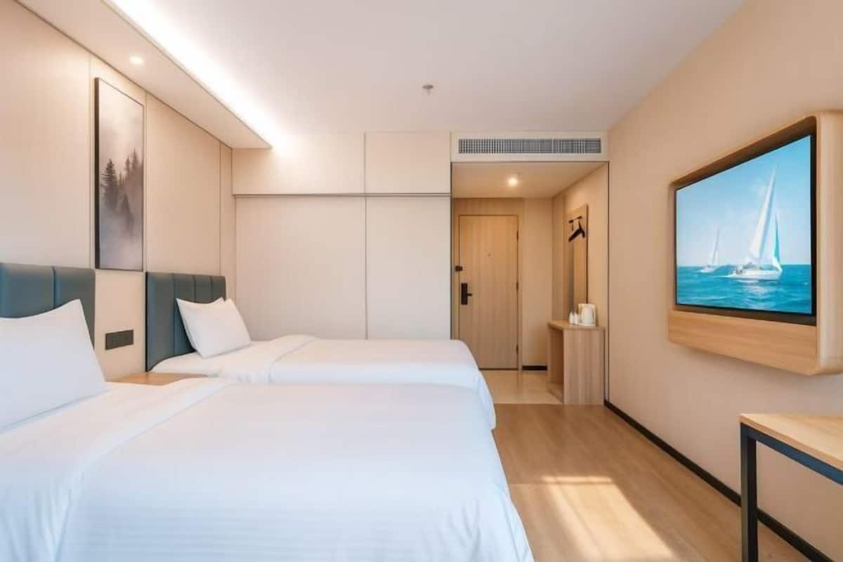 Quarto de hotel com duas camas, uma televisão grande e uma porta para o banheiro.
