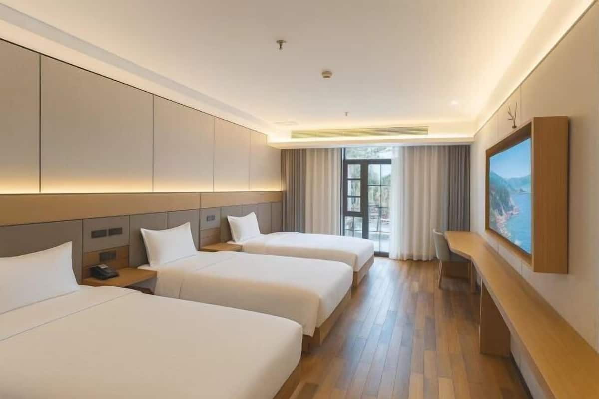 Quarto de hotel com duas camas, uma escrivaninha, uma televisão e uma janela grande.